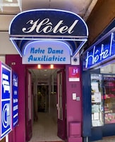 Entrada de hotel com um letreiro de neon que diz "Hotel Notre Dame Auxiliatrice" e número de quarto visível "28".