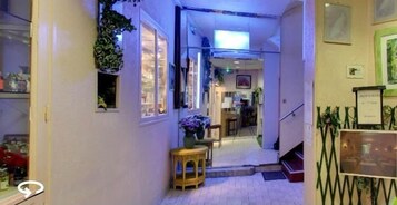 Um corredor estreito com um banco de madeira, uma mesa pequena com flores e uma escadaria que leva a outro cômodo.
