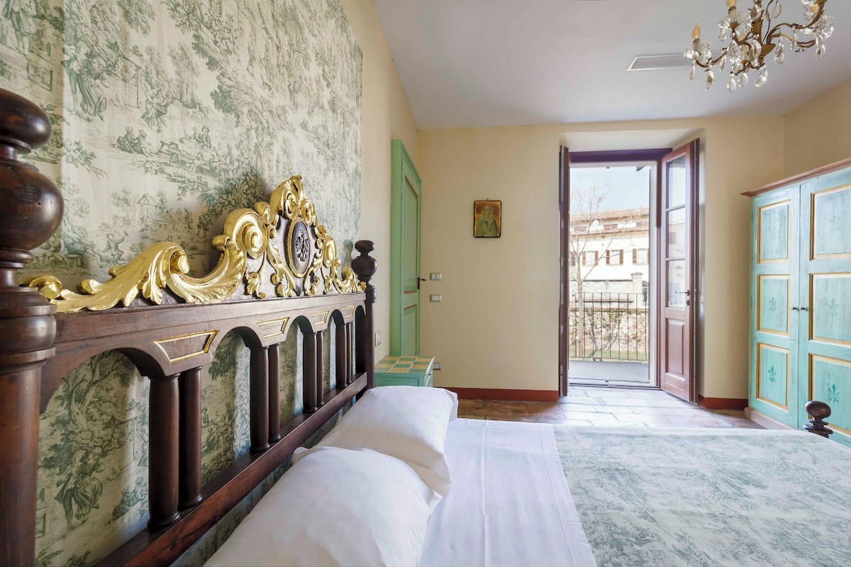 Quarto de hotel com uma cama, cabeceira de madeira, porta verde e vista para o exterior.