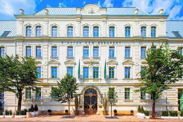 Um edifício grande e clássico, com fachada simétrica, várias janelas e uma entrada central com arco decorativo.