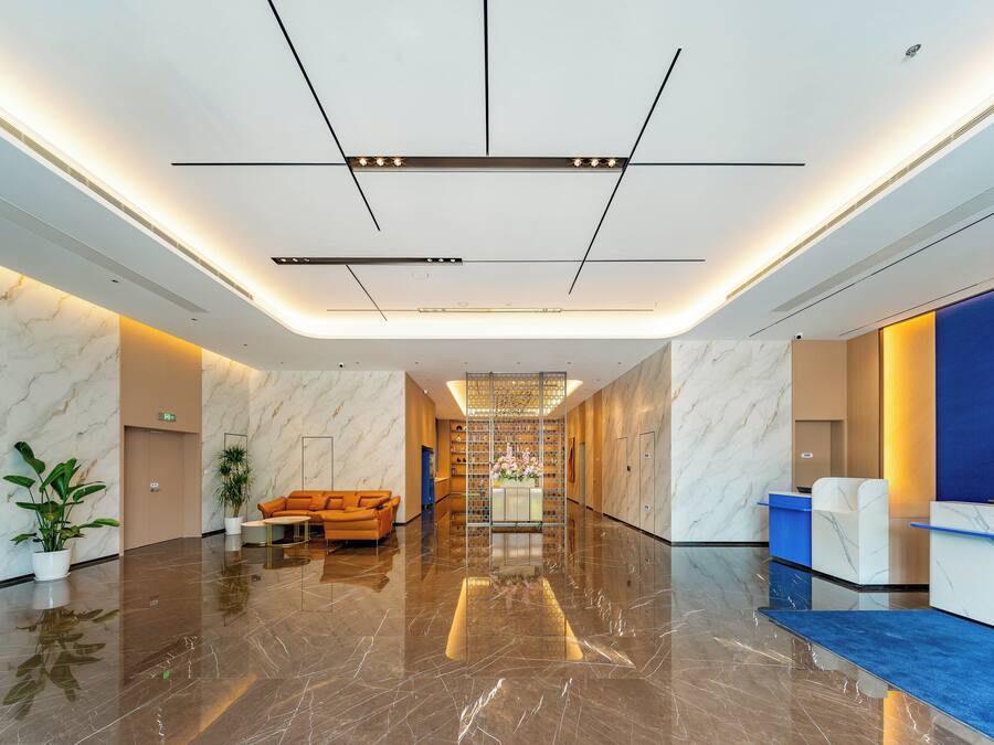 Um hall amplo com piso de mármore, um balcão de recepção, uma área de estar com sofá e um lustre decorativo.