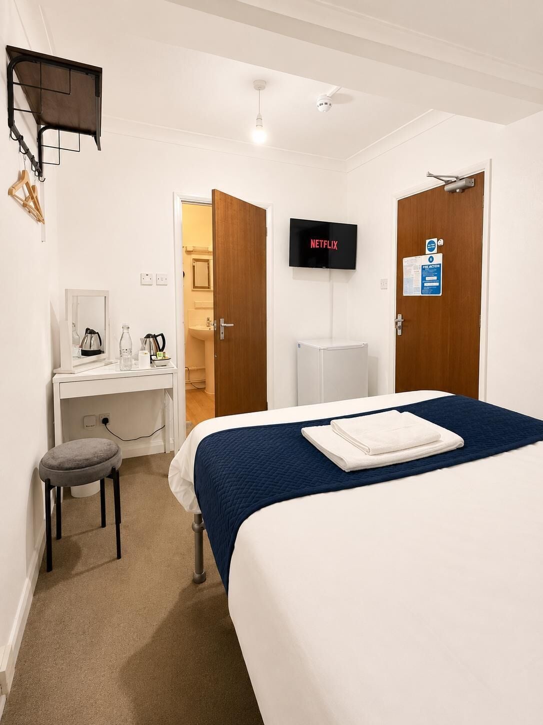 Quarto de hotel com uma cama, uma escrivaninha, uma cadeira, uma televisão e uma porta.