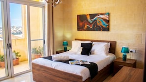 Quarto com cama, duas mesas de cabeceira, um quadro na parede e vista através de uma porta deslizante.