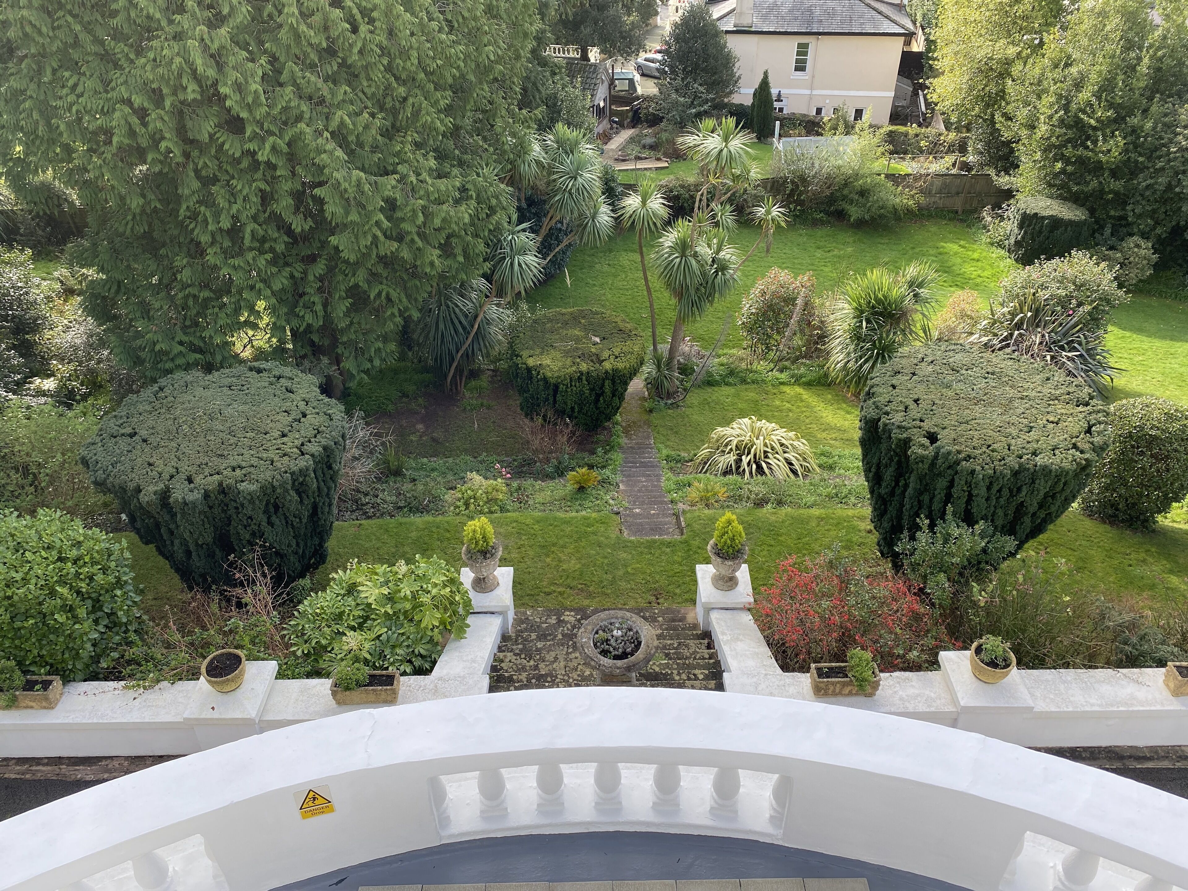 Um jardim com um caminho, sebes aparadas e um balaustrada branca.