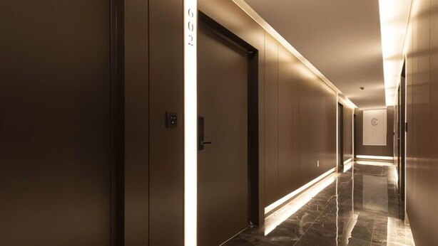 Corredor moderno de hotel com piso de mármore, portas de madeira escura e iluminação embutida.