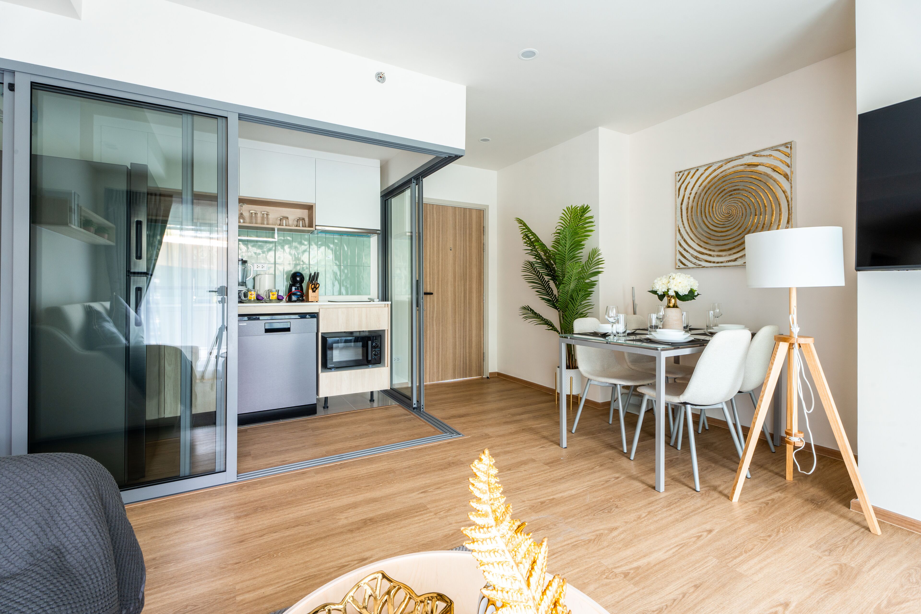 Uma sala de estar moderna com um sofá, uma mesa de jantar com cadeiras, um abajur e uma TV fixada na parede.