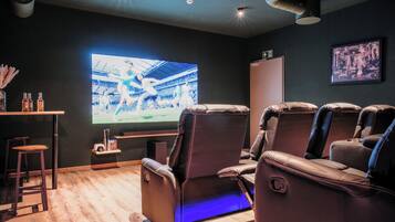 Um home theater com poltronas reclináveis de couro, uma TV grande de tela plana e piso de madeira.