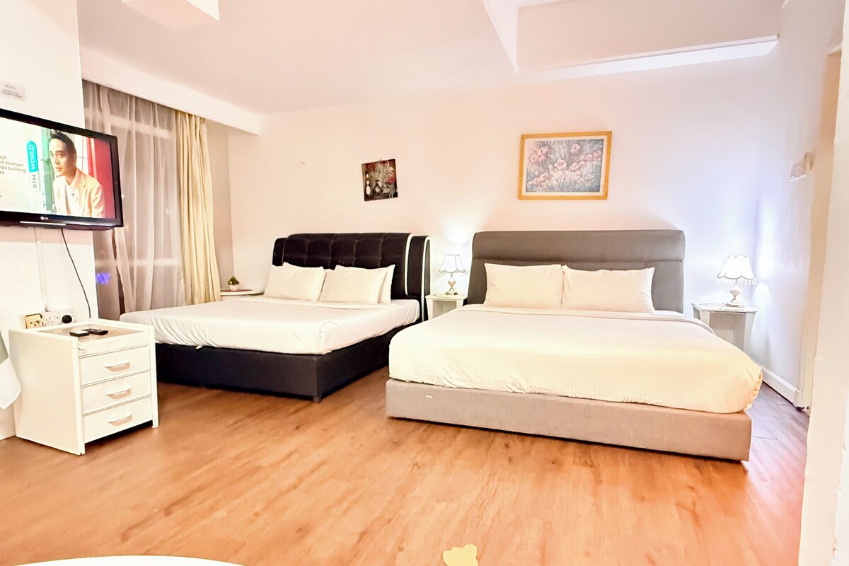 Quarto de hotel com duas camas, televisão, mesa pequena e mesa de cabeceira.