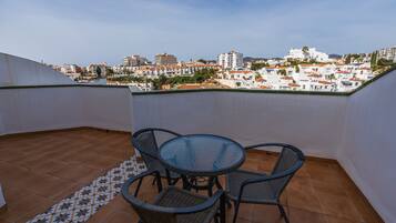 Um terraço com uma mesa redonda e quatro cadeiras, com vista para uma área residencial com edifícios brancos e telhados vermelhos.