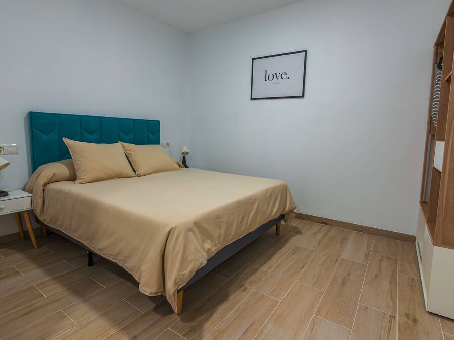 Quarto com cama, mesa de cabeceira, luminária e um quadro pendurado na parede.