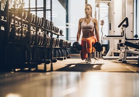 Interior de academia com equipamentos de exercícios, incluindo halteres e bancos.