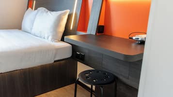Quarto de hotel moderno com uma cama, um banquinho pequeno e uma escrivaninha com abajur.