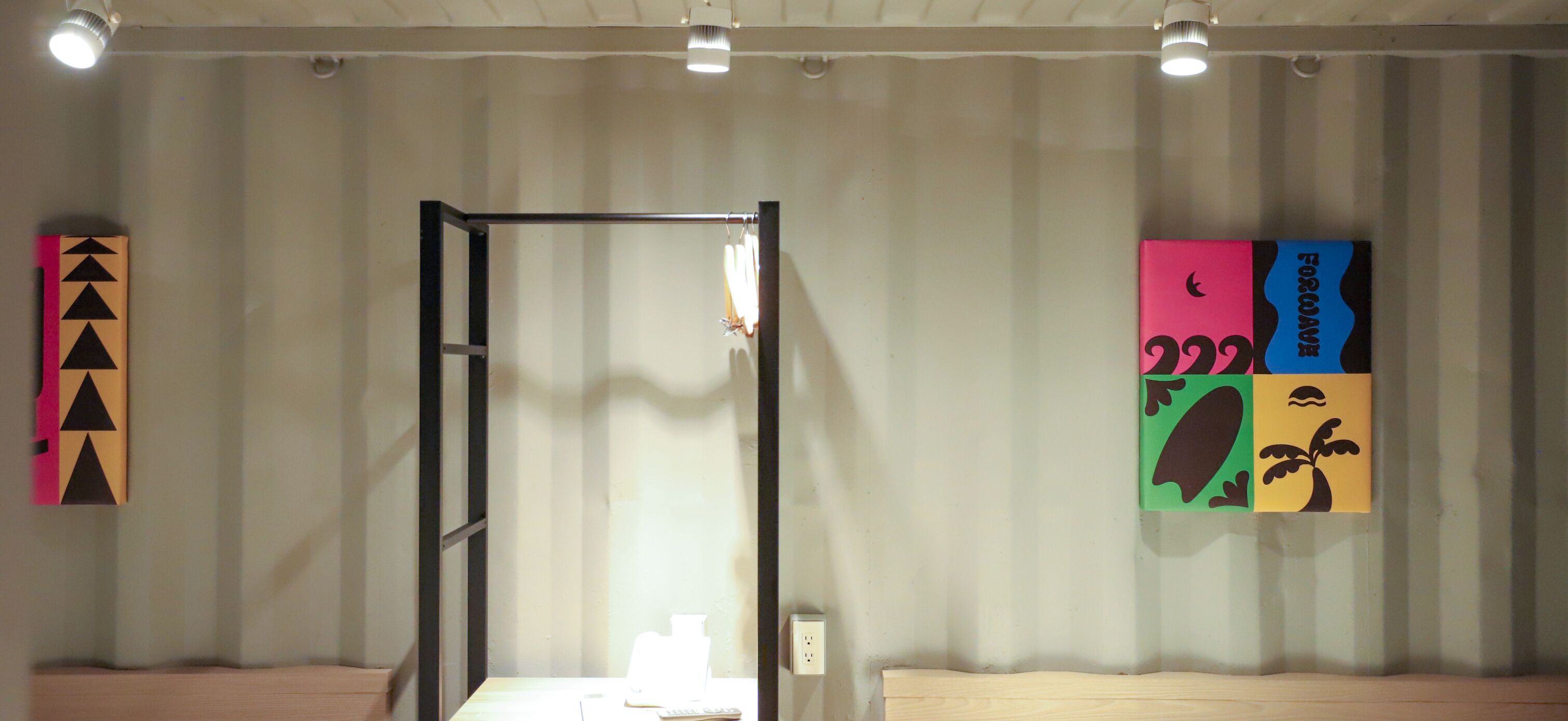 Quarto com estrutura de metal, uma mesa branca com teclado e arte abstrata nas paredes.
