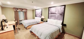 Quarto de hotel com duas camas, uma escrivaninha, uma cadeira, uma luminária e uma janela grande com vista.