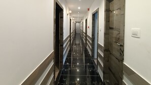 Corredor de hotel com piso preto polido, paredes brancas e portas em ambos os lados.