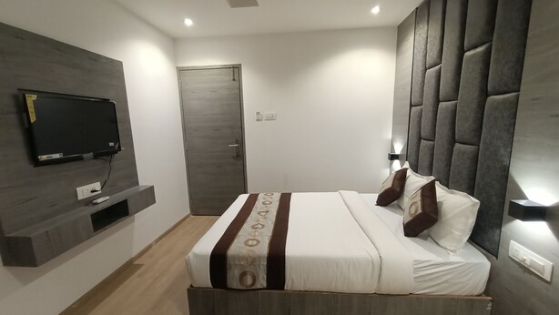 Quarto moderno com uma cama grande, televisão montada e cabeceira de madeira.