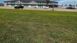 Um motel com estacionamento, um campo gramado e uma palmeira.