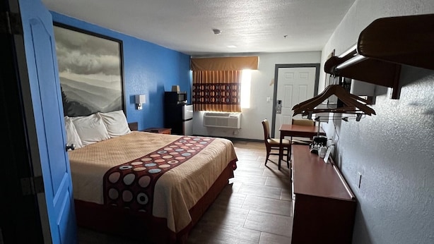 Quarto com uma cama, uma escrivaninha e uma cadeira. Há uma janela com cortinas e uma porta.