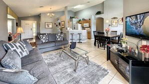 Uma sala de estar moderna com um sofá cinzento, uma mesa de centro de vidro e um espaço de jantar com uma mesa e cadeiras de madeira.