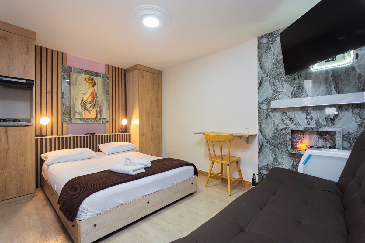 Quarto moderno com cama, escrivaninha de madeira, poltrona, TV na parede e lareira.