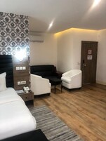 Quarto de hotel com cama, sofá, poltrona, mesa de cabeceira com telefone e porta com placa de proibido fumar.