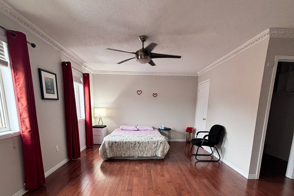 Um quarto espaçoso com piso de madeira, uma cama, um ventilador de teto e uma escrivaninha com cadeira.