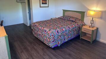 Um quarto com cama, mesa de cabeceira, luminária e um quadro na parede.