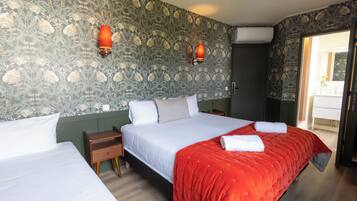 Quarto de hotel com uma cama grande, uma mesa de cabeceira, uma luminária na parede e uma porta para o banheiro.