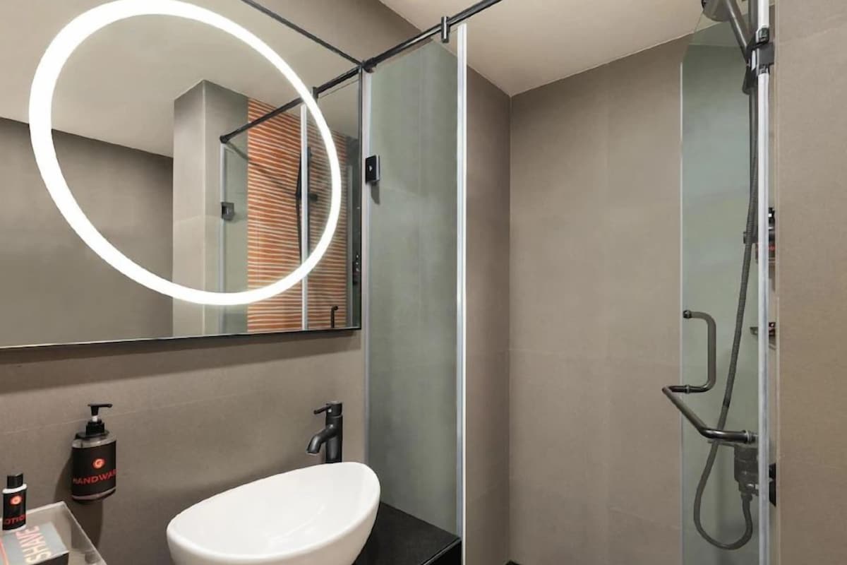 Uma casa de banho moderna com um espelho grande, uma sanita branca e um chuveiro com parede de vidro.
