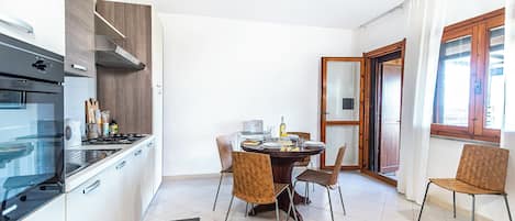 Cozinha compacta com eletrodomésticos modernos, área de refeições com quatro cadeiras e vista através de uma porta aberta.