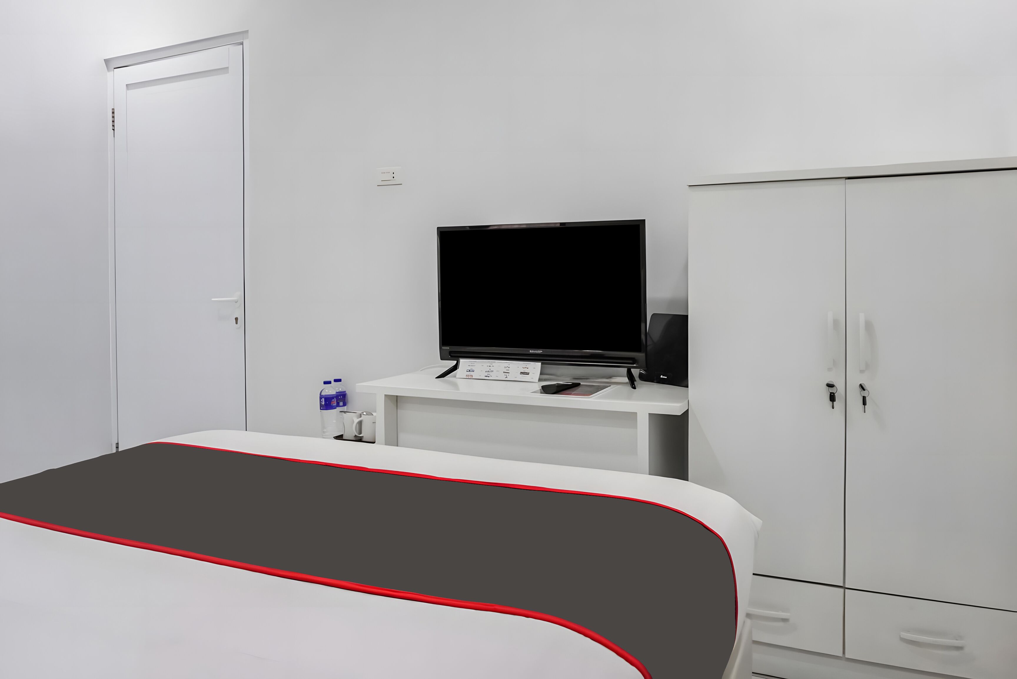 Quarto de hotel com uma cama, uma escrivaninha com computador, um guarda-roupa e uma porta.