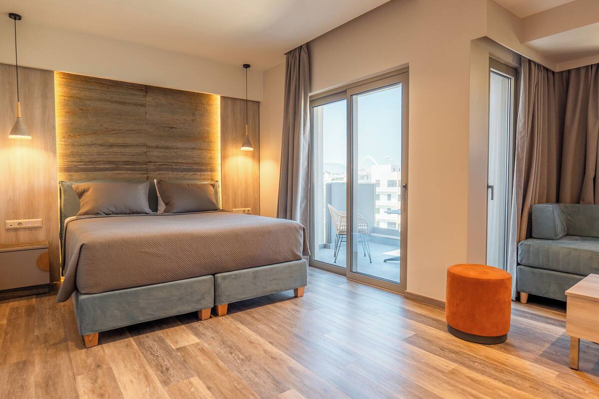 Quarto moderno com uma cama grande, um sofá e um banquinho laranja.