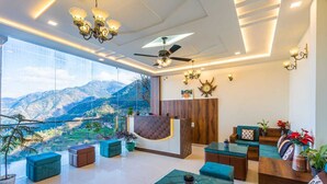 Quarto amplo com grande janela com vista para as montanhas, uma mesa de recepção e móveis modernos.