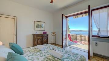 Quarto com cama, cômoda, ventoinha no teto e varanda com vista para o mar.