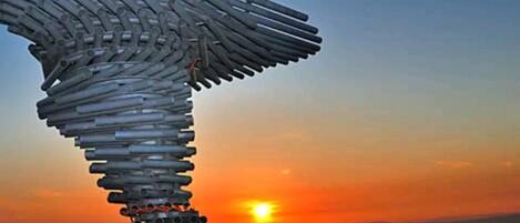 Escultura de tubos e barras de metal formando uma estrutura em espiral ao pôr do sol.