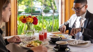 Uma mesa de jantar com pratos de comida, um vaso de flores e um copo de bebida vermelha.