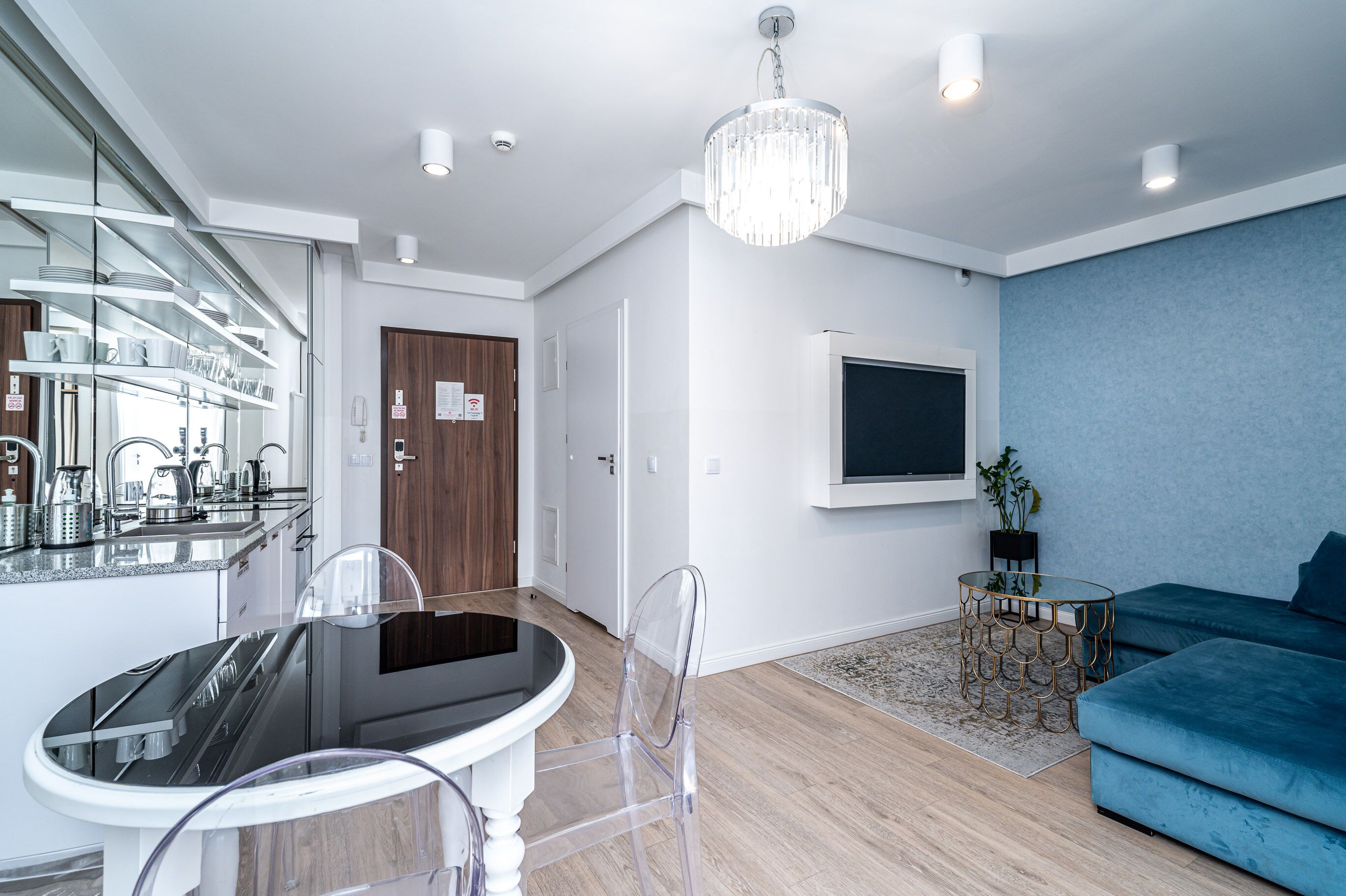 Uma cozinha moderna com área de refeições, uma sala de estar com sofá azul e um candelabro.
