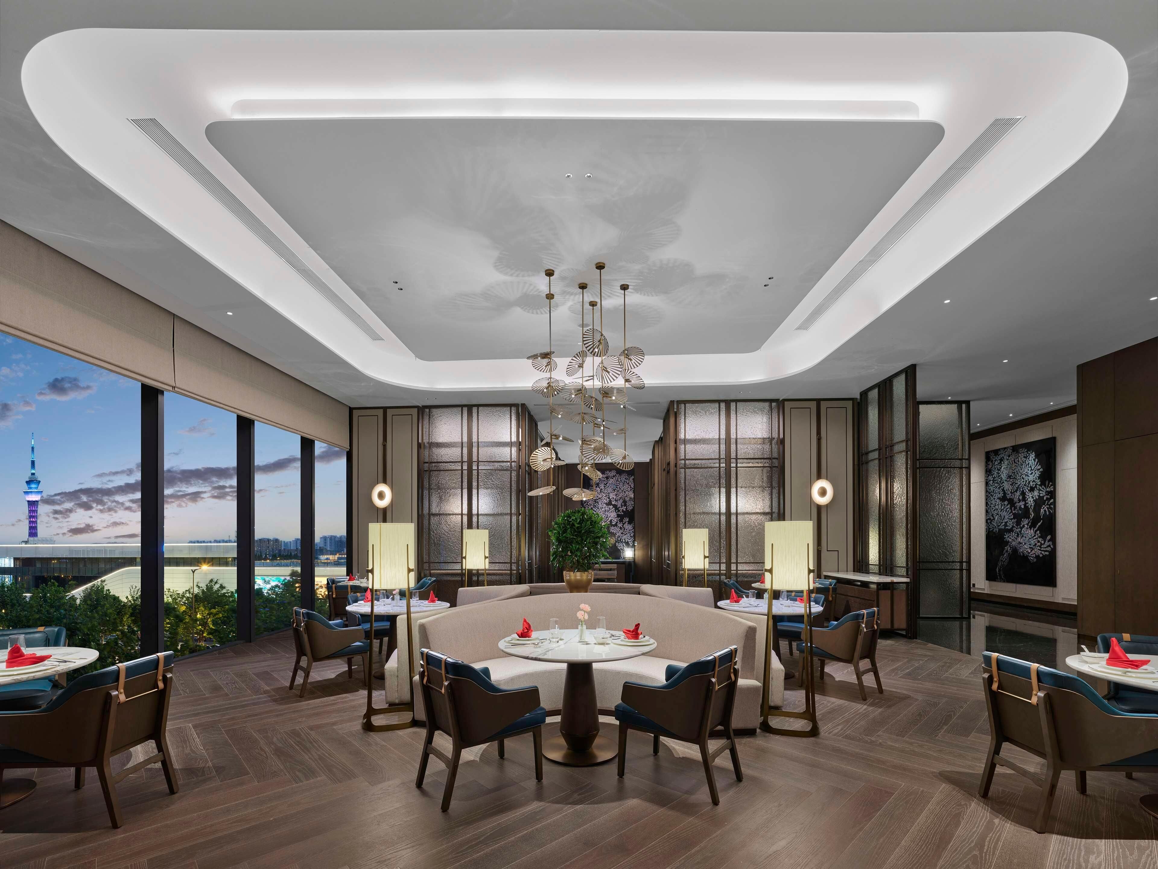 Uma sala de jantar moderna com uma mesa redonda, várias cadeiras e iluminação pendente.