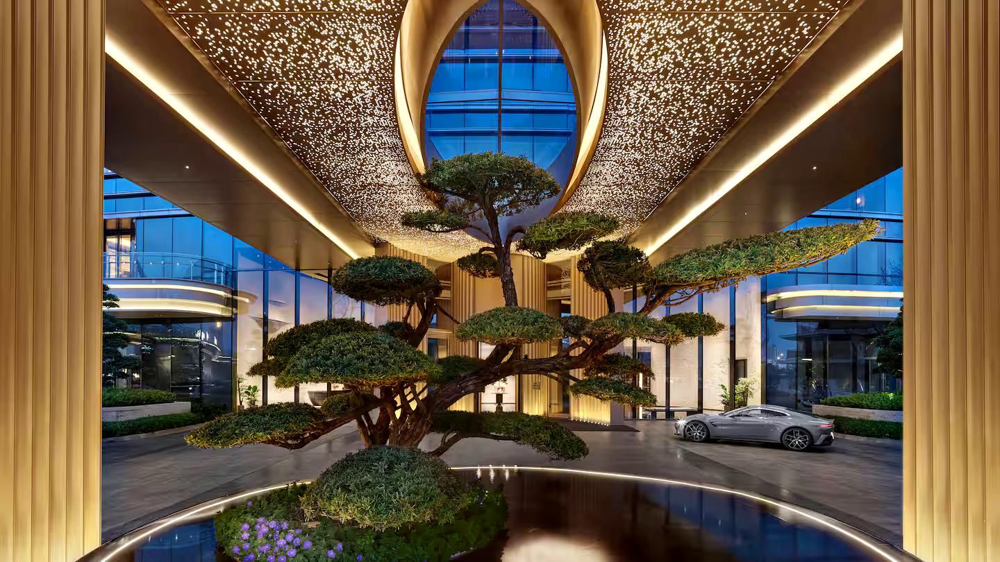 Um lobby moderno com uma grande árvore, um carro e um elemento aquático refletivo.