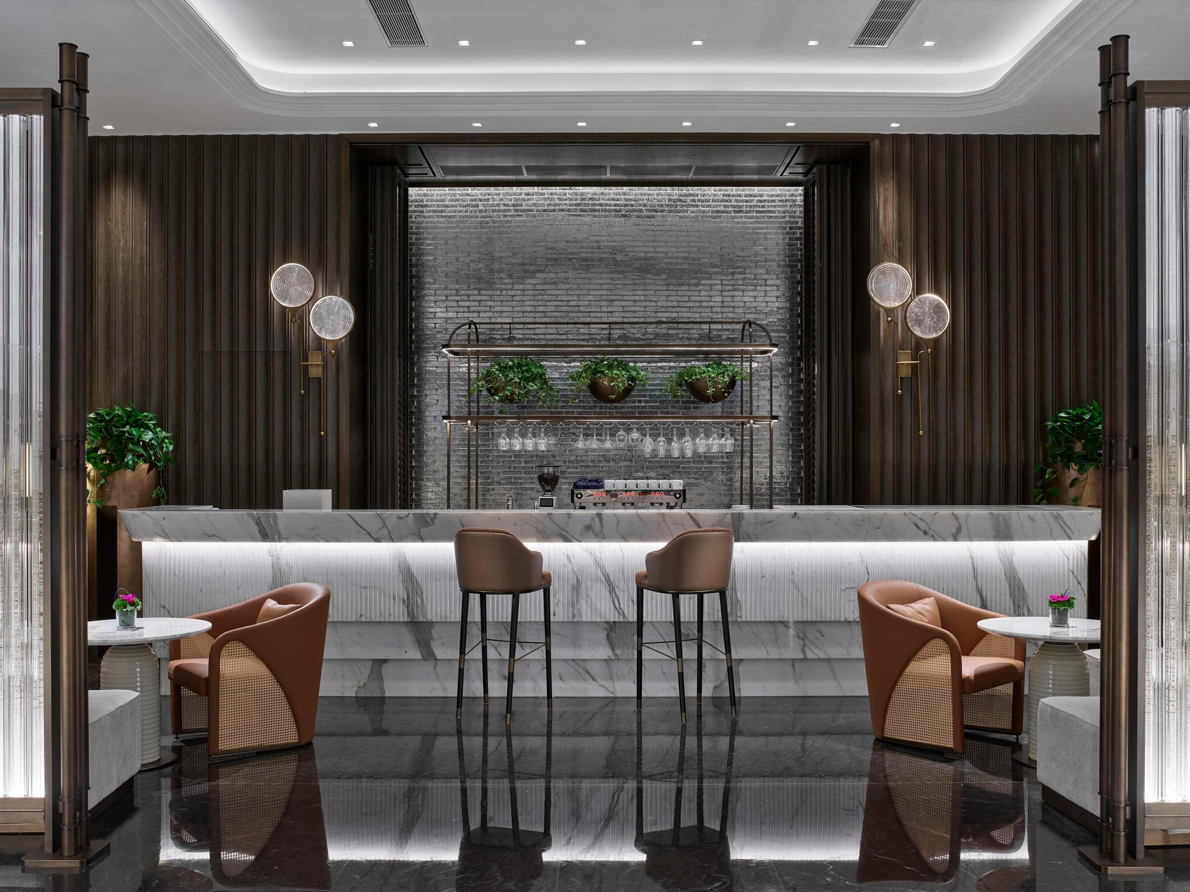 Uma área de bar moderna com bancada de mármore, dois bancos altos e parede de tijolos ao fundo.