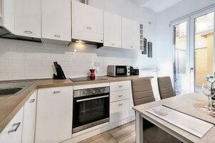 Uma cozinha moderna com armários brancos, forno embutido, micro-ondas e uma área de jantar com mesa e cadeiras.