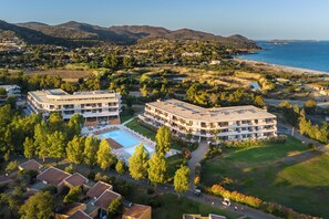 Um hotel com vários andares, piscina, rodeado por vegetação e montanhas.