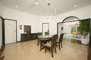 Uma sala de jantar moderna com uma mesa redonda, cadeiras, ventiladores de teto e um vaso de planta.