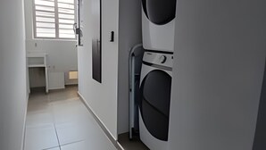Uma lavanderia com duas máquinas de lavar empilhadas, uma janela e uma porta que dá para outro cômodo.