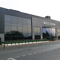 Um edifício moderno com grandes janelas e a inscrição 'MILL FARM' na fachada.