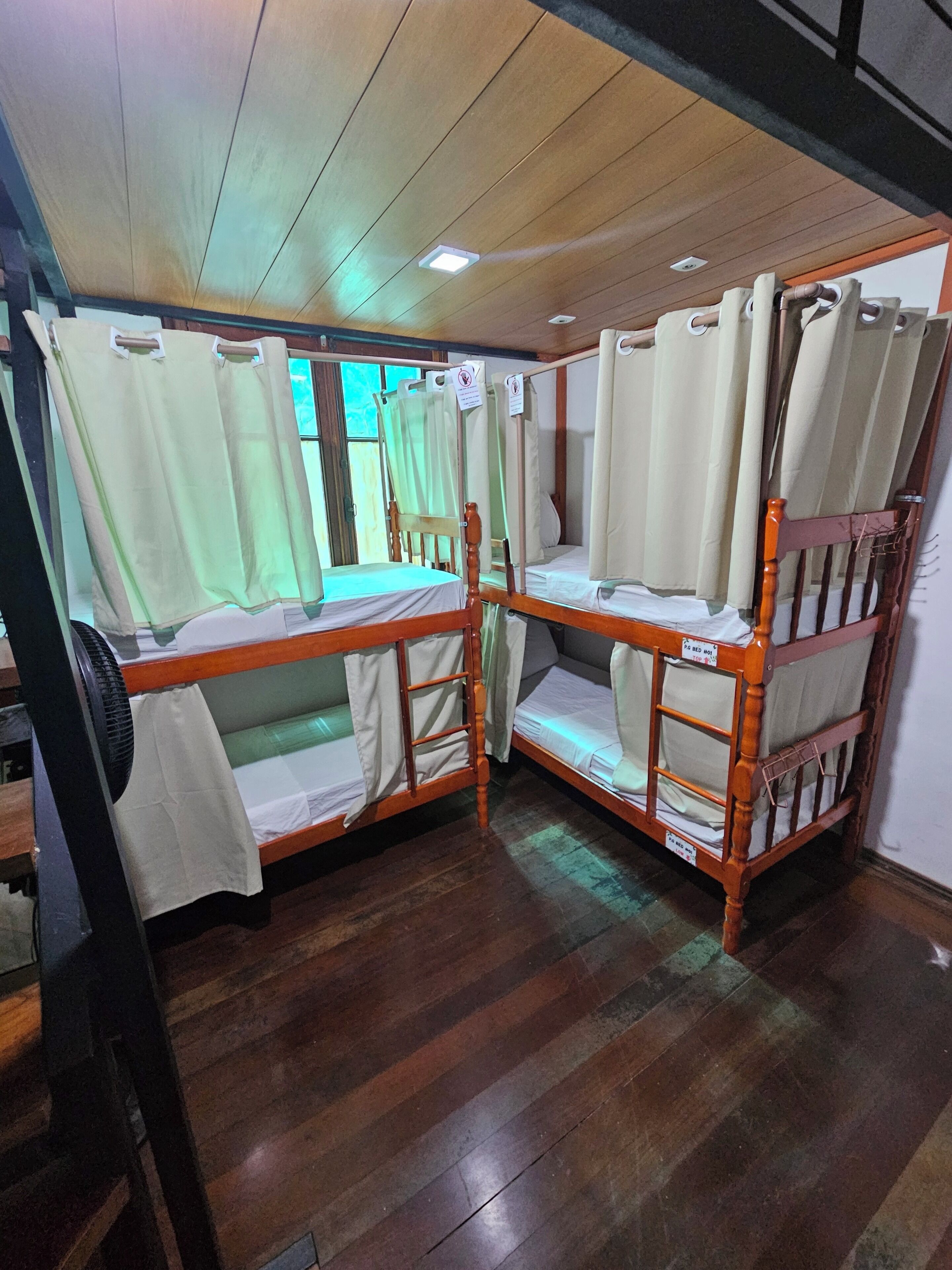 Quarto com beliches de madeira, cada um com colchão e travesseiro. Há uma escada entre as camas para acesso.