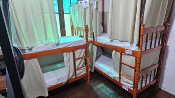 Quarto com beliches de madeira, cada um com colchão e travesseiro. Há uma escada entre as camas para acesso.