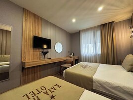 Quarto de hotel com cama, escrivaninha, televisão na parede e janela com cortinas.