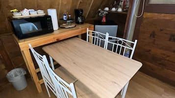 Uma pequena cozinha compacta com micro-ondas, cafeteira e diversos utensílios.