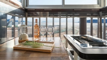 Uma cozinha com vista para a paisagem costeira, uma garrafa de vinho, duas taças de vinho, um fogão portátil e uma tábua de corte de madeira com uma folha.